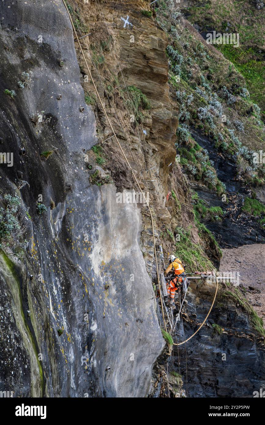 A worker suspended by ropes working to stabilise stabilize the cliff ...