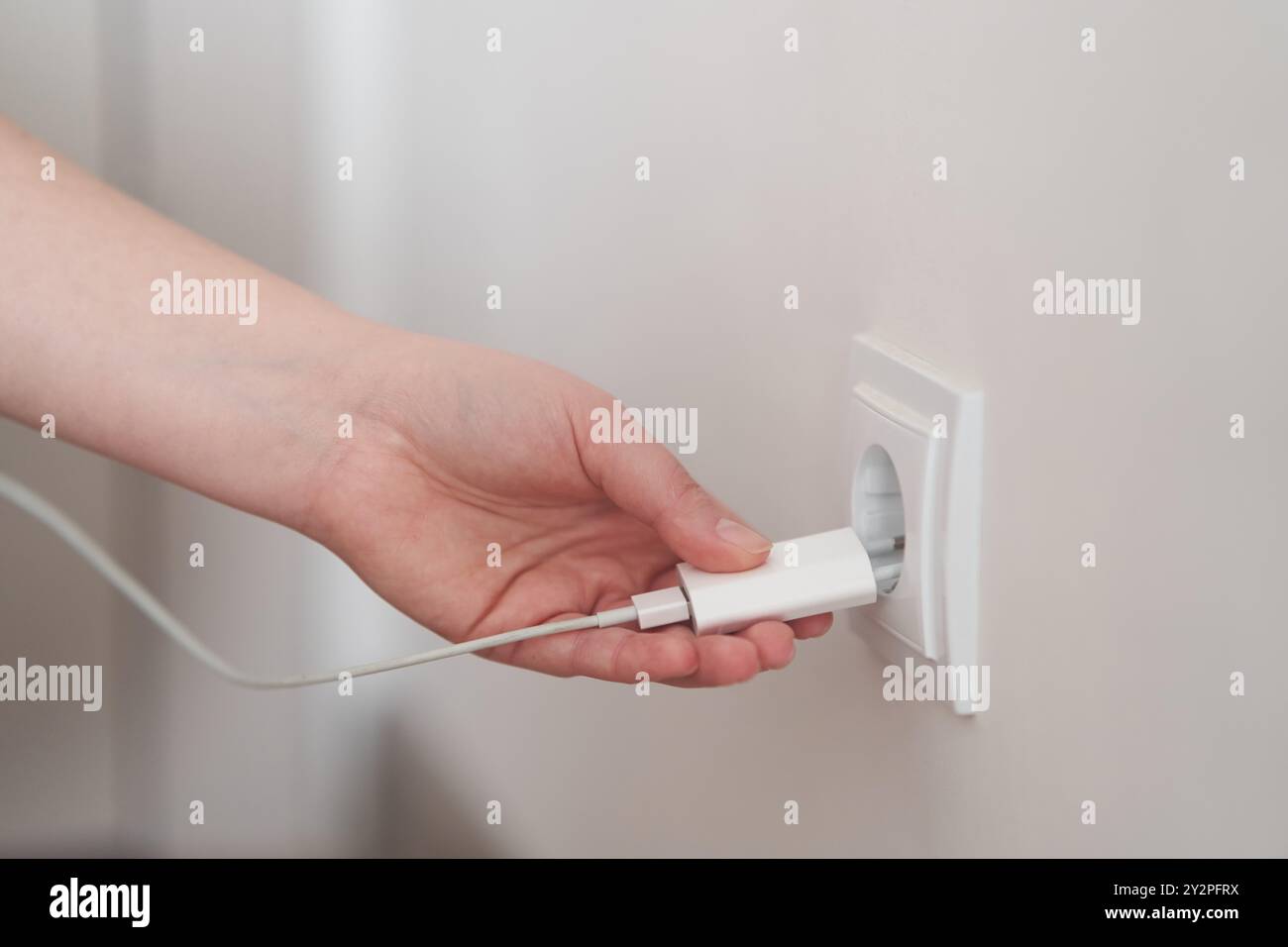 A young girl inserts a plug into an outlet. Young woman plugs the phone ...