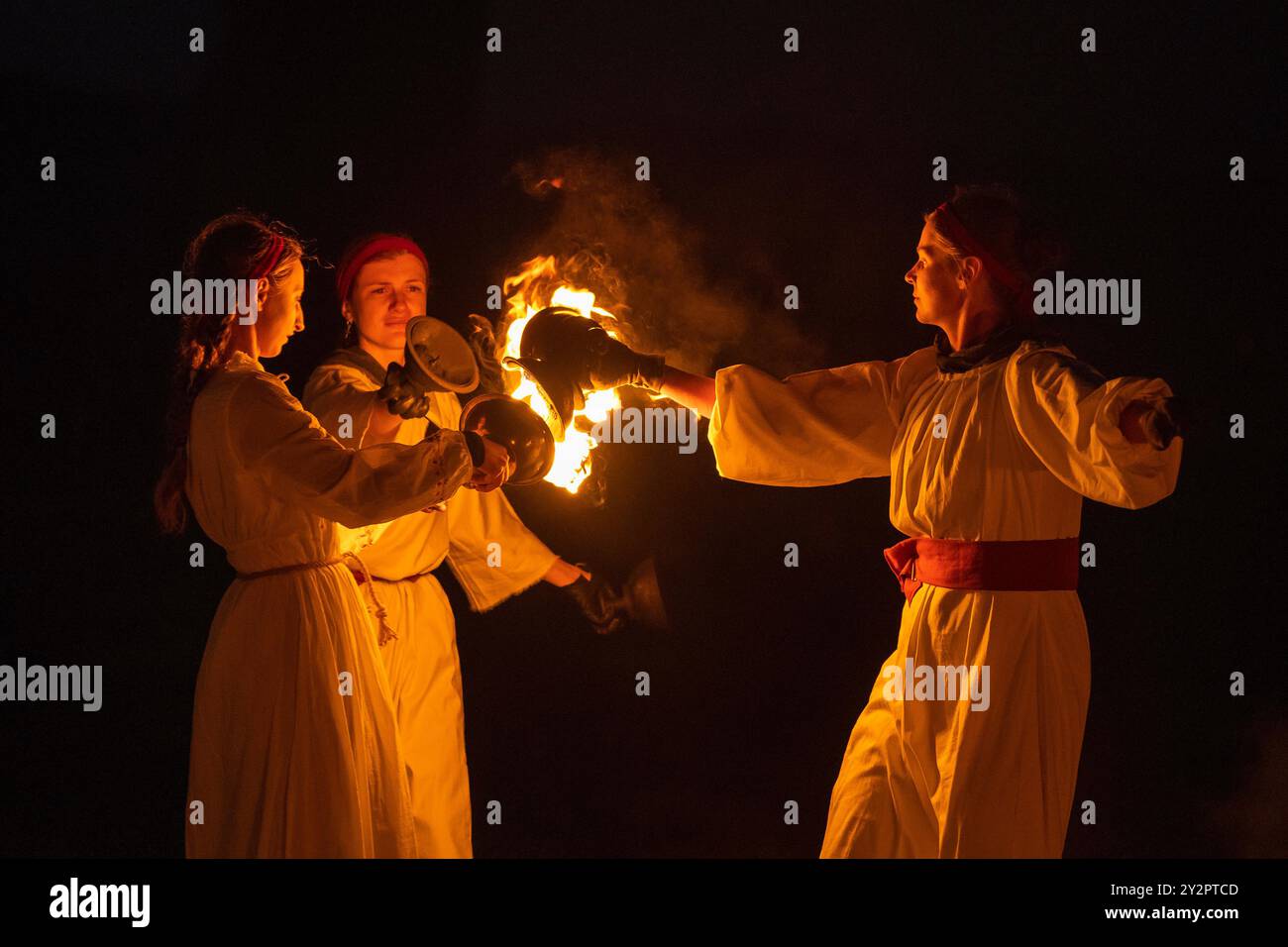 TVER REGION, RUSSIA - JULY 21, 2023: Three girls in ancient clothes light a fire on a dark night ...