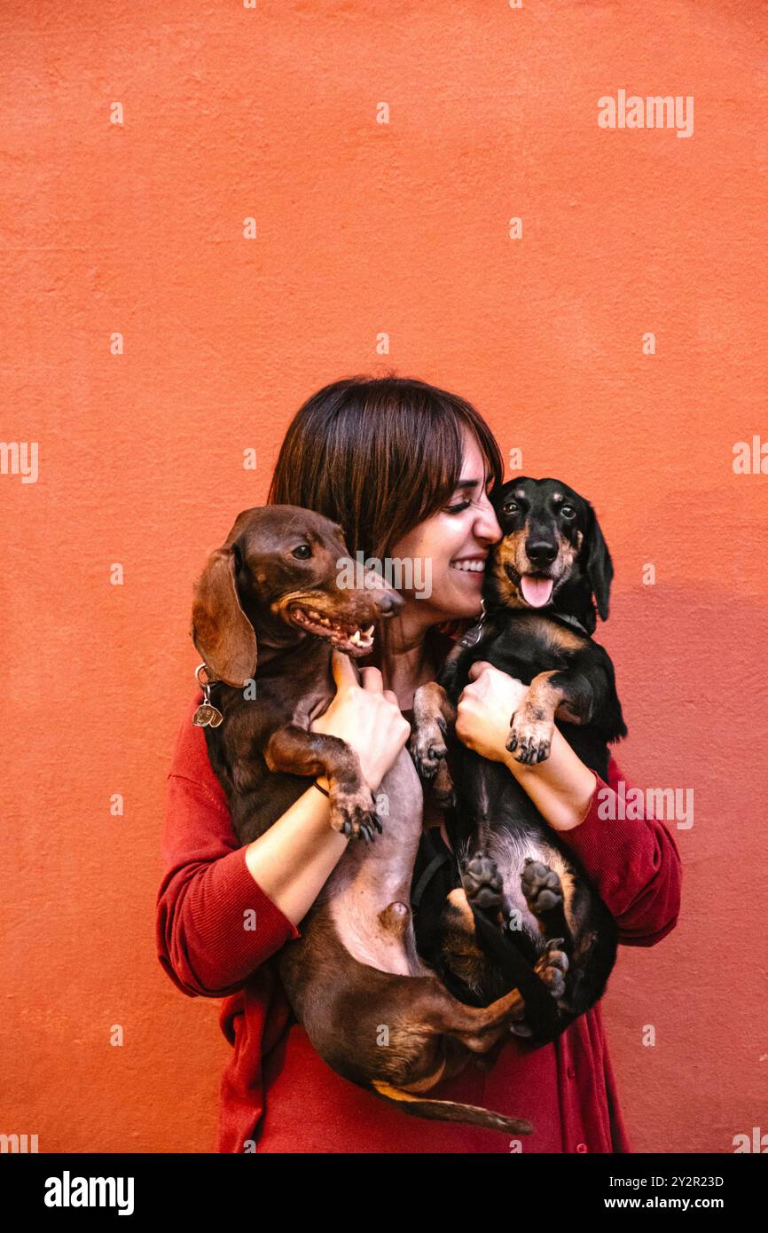 A joyful young woman, smiling broadly, embraces two Teckel dogs against ...