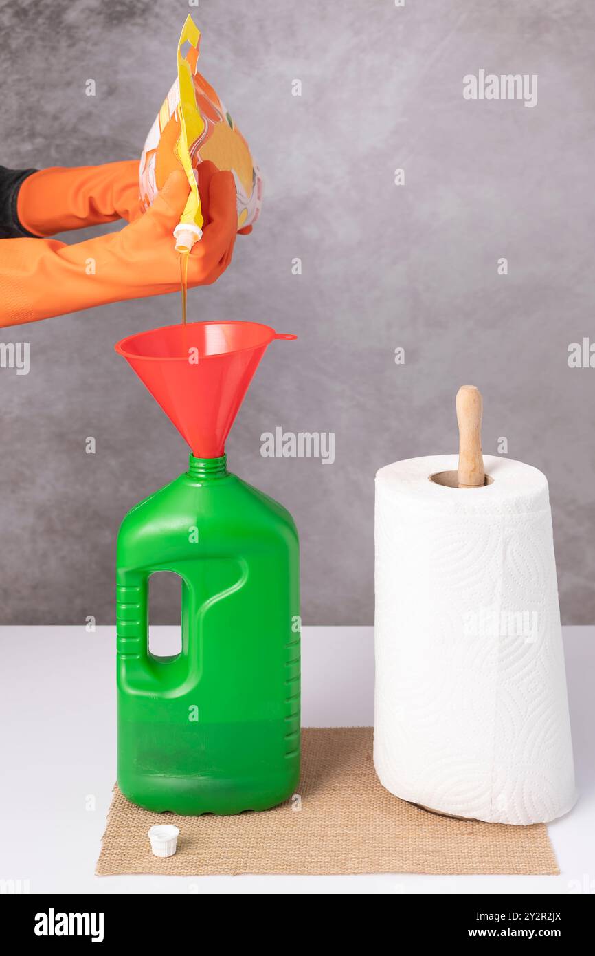 A green plastic bottle is filled with dishwashing liquid from a refill ...