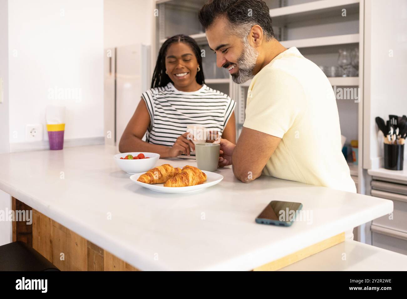 A cheerful multiracial couple shares a pleasant breakfast moment in a ...