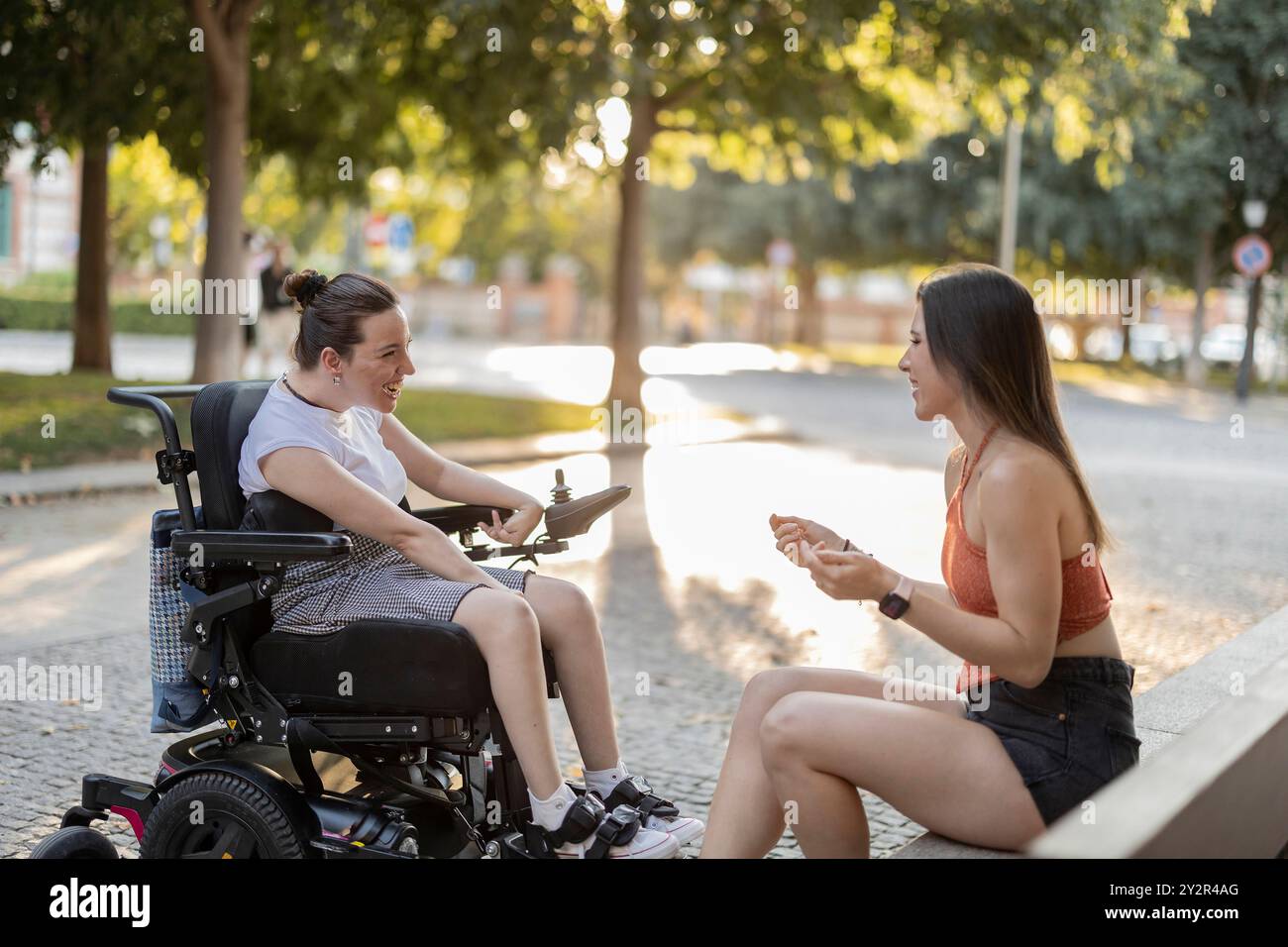 Two young women enjoy a heartfelt talk in a park; one is seated in a ...