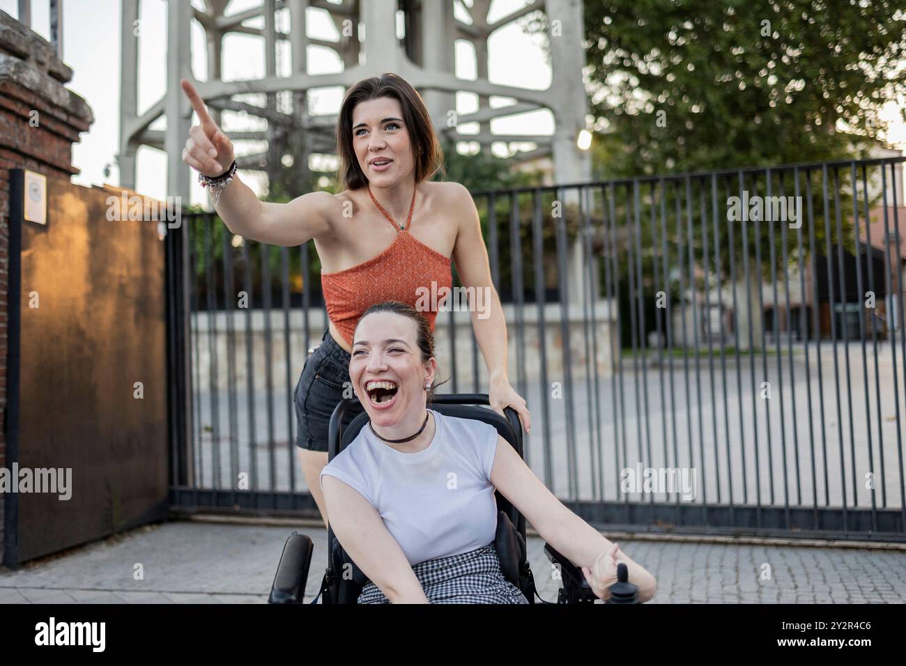 Two young women share a joyful moment outdoors; one points and laughs ...