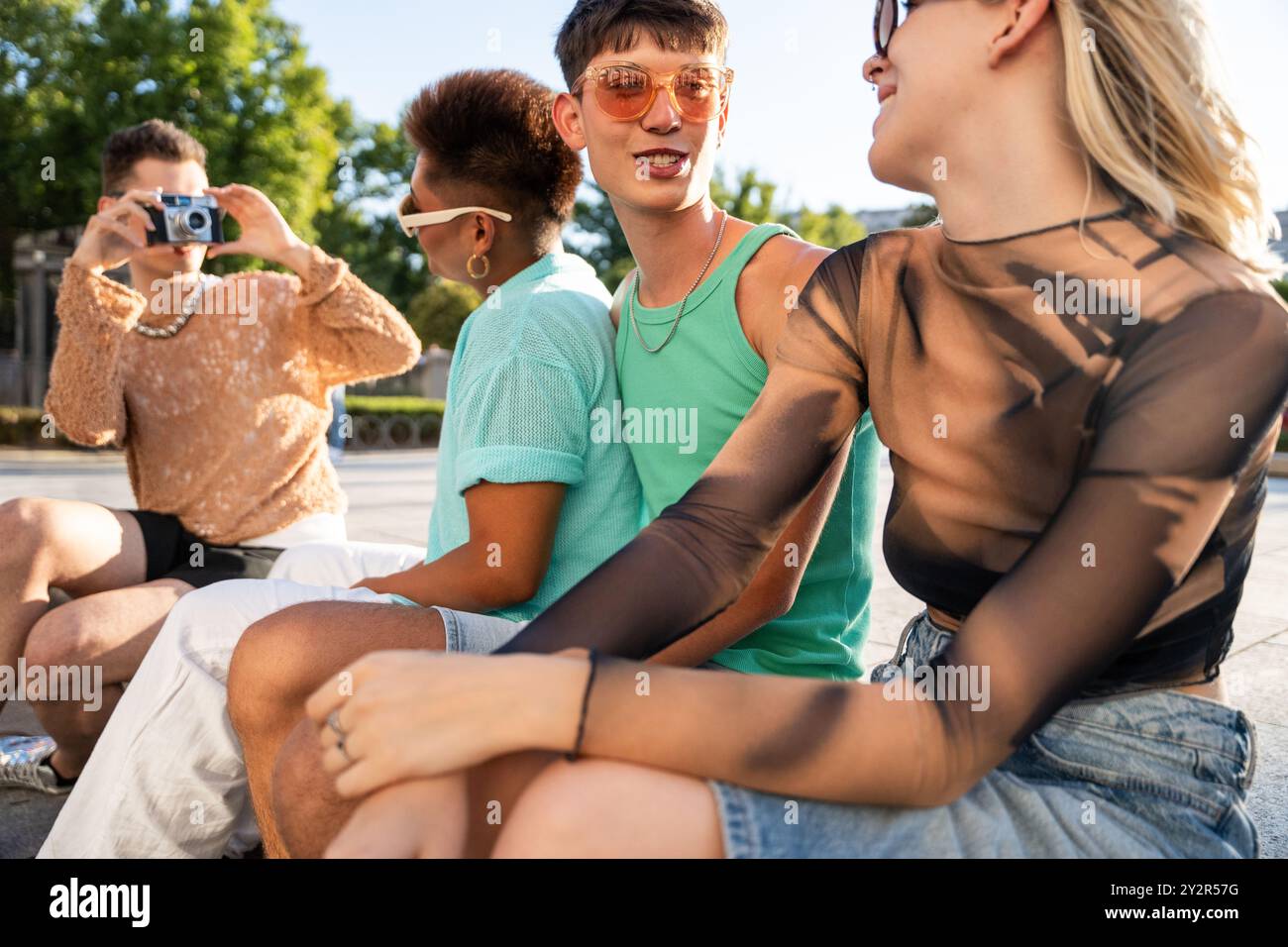 Joyful LGBTQIA+ friends share a laugh outdoors, one capturing the moment with a camera Stock ...