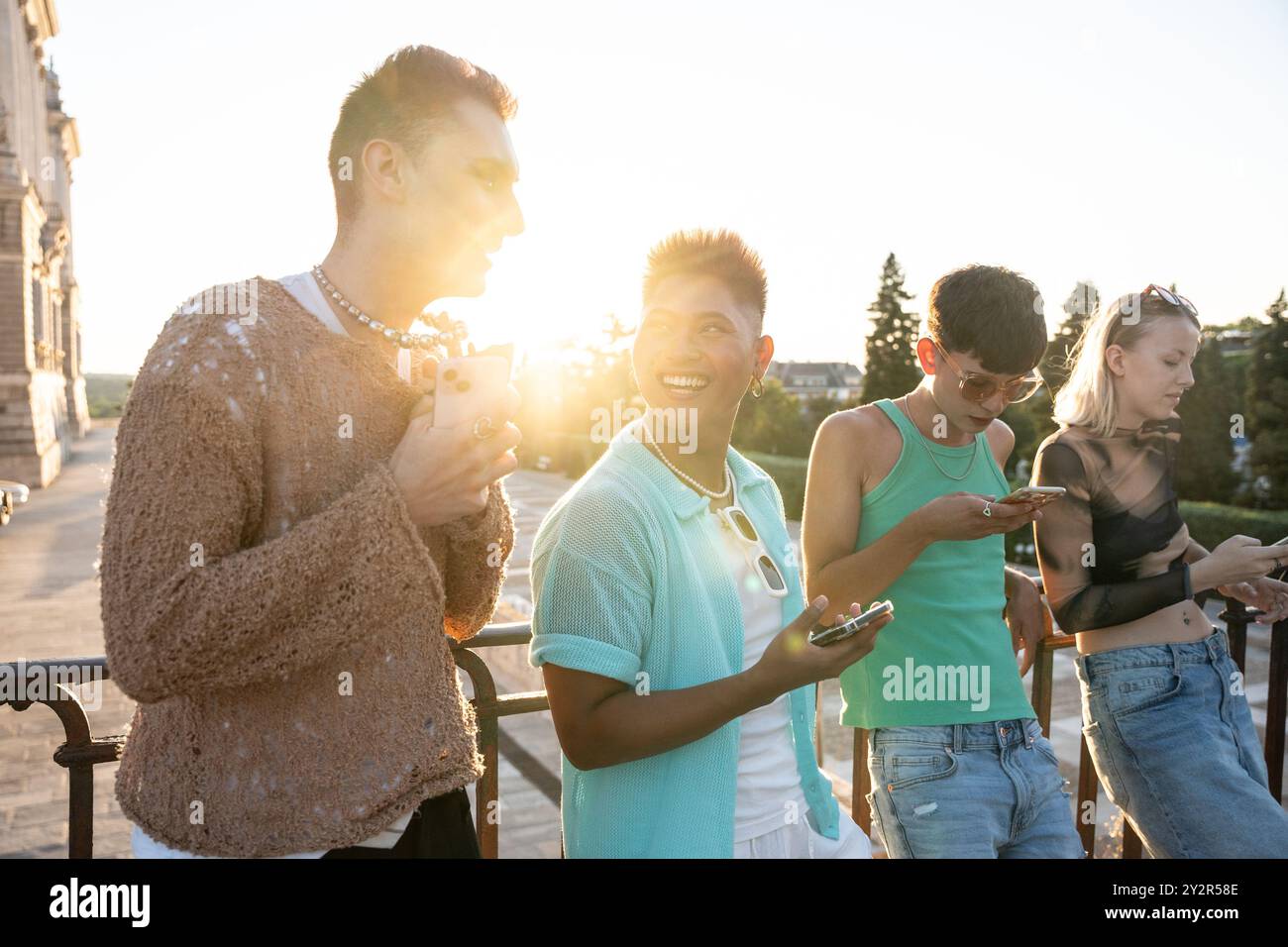 A diverse group of LGBTQIA+ friends smiling, chatting, and using smartphones while enjoying a ...