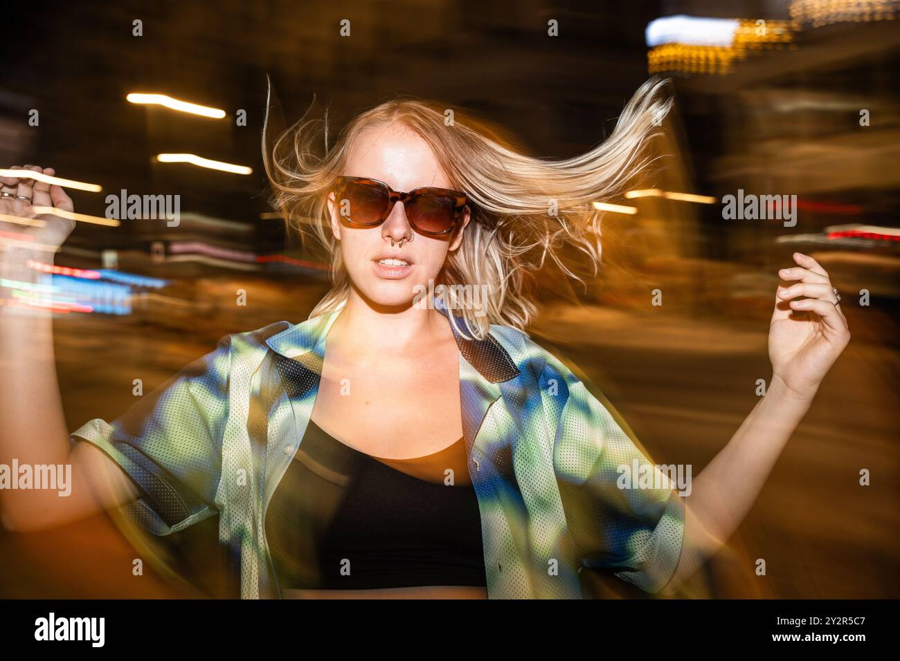 A stylish young woman strikes a pose on a city street at night, with ...