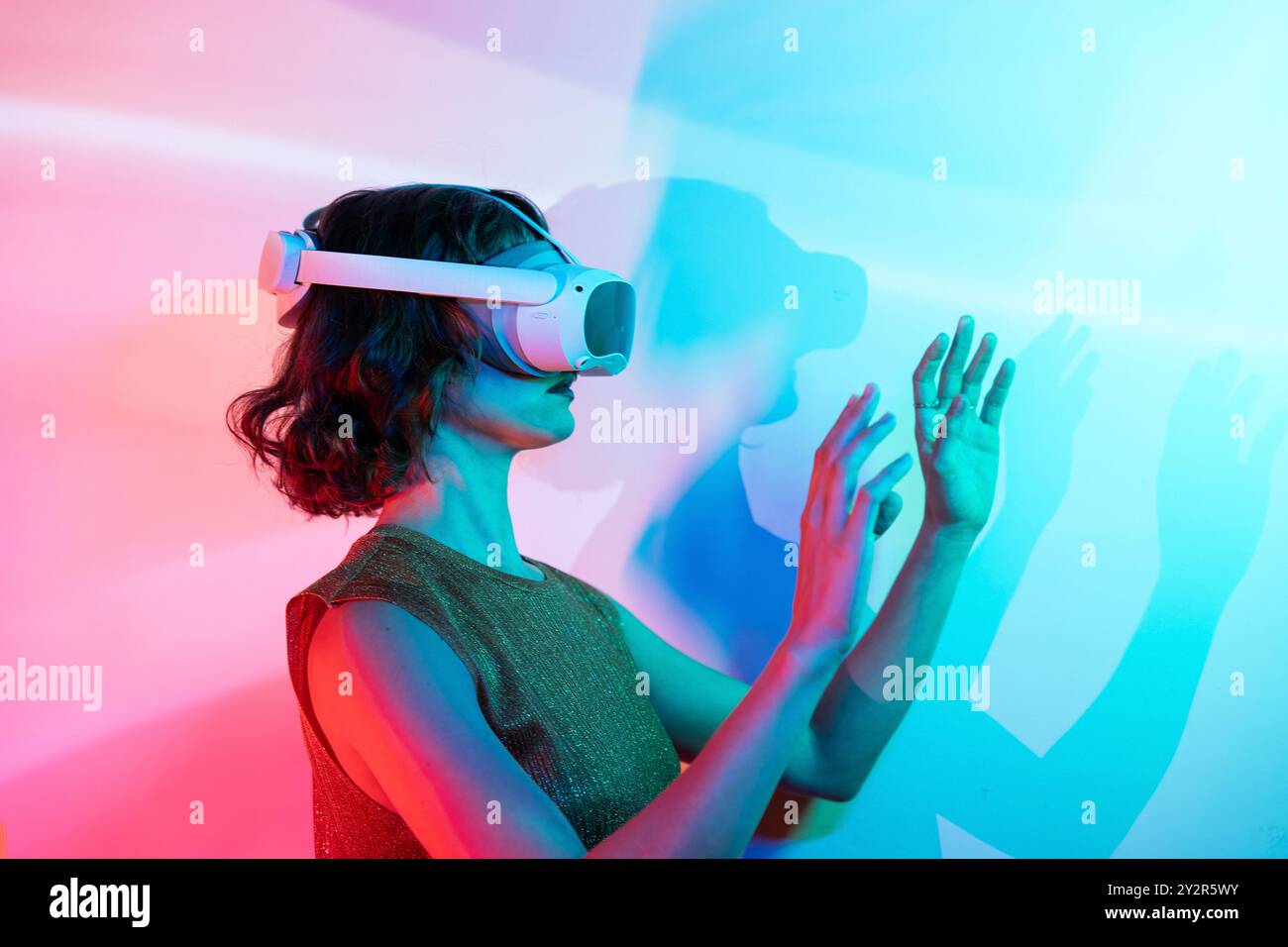 A woman engages with a virtual reality headset, her figure bathed in ...