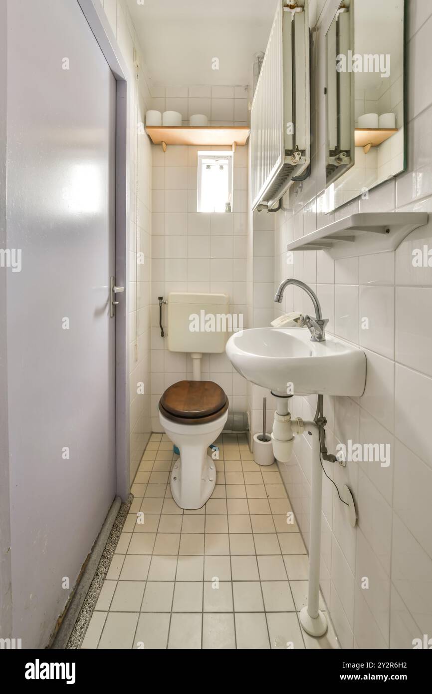 Interior view of a small, white-tiled bathroom with a toilet and ...