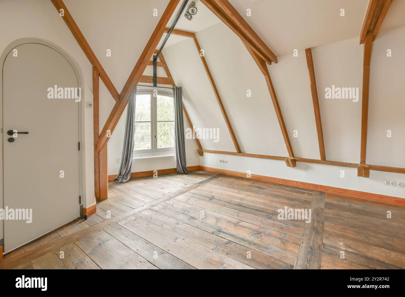 Empty attic room featuring exposed wooden beams, hardwood flooring, and ...