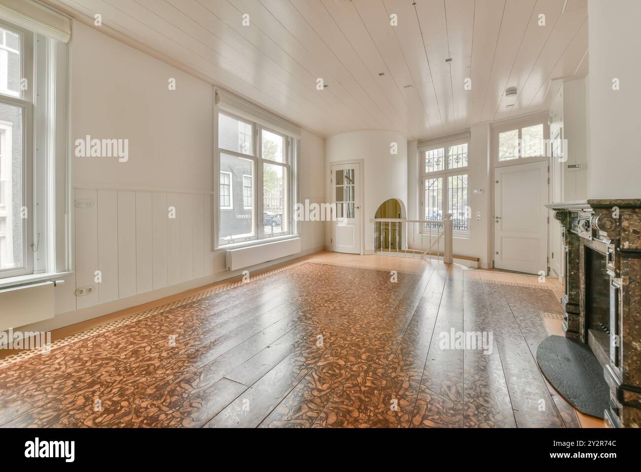 An empty, well-lit room featuring large windows, white walls, and an ...