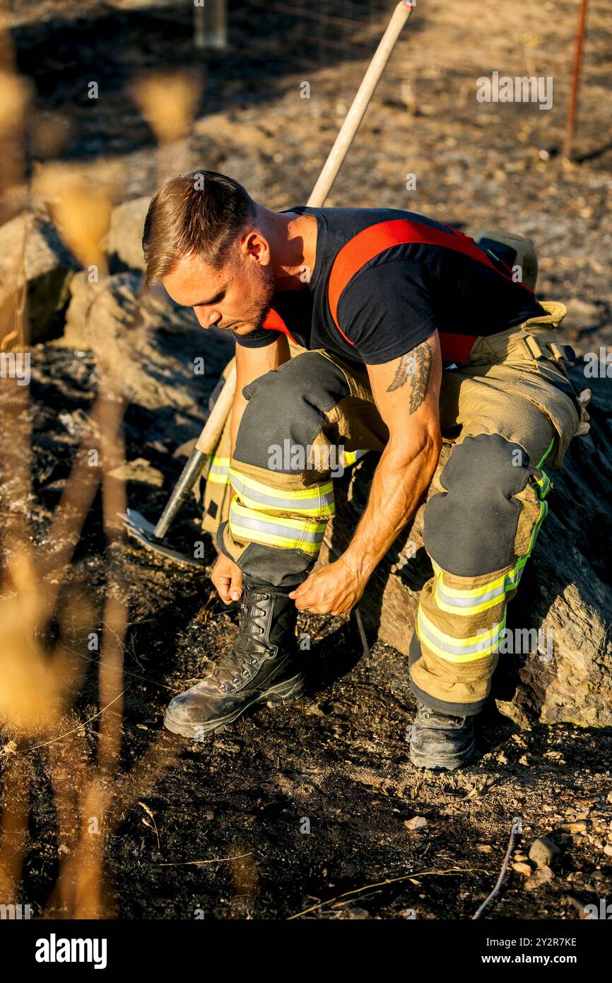A firefighter tightens his boots while kneeling in a dry, rugged ...
