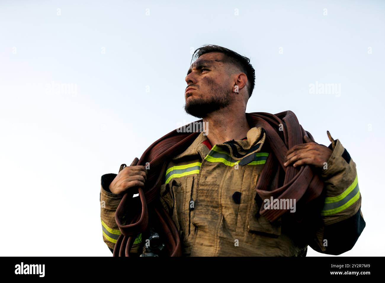 A gritty photo of a firefighter with a hose slung over his shoulder ...