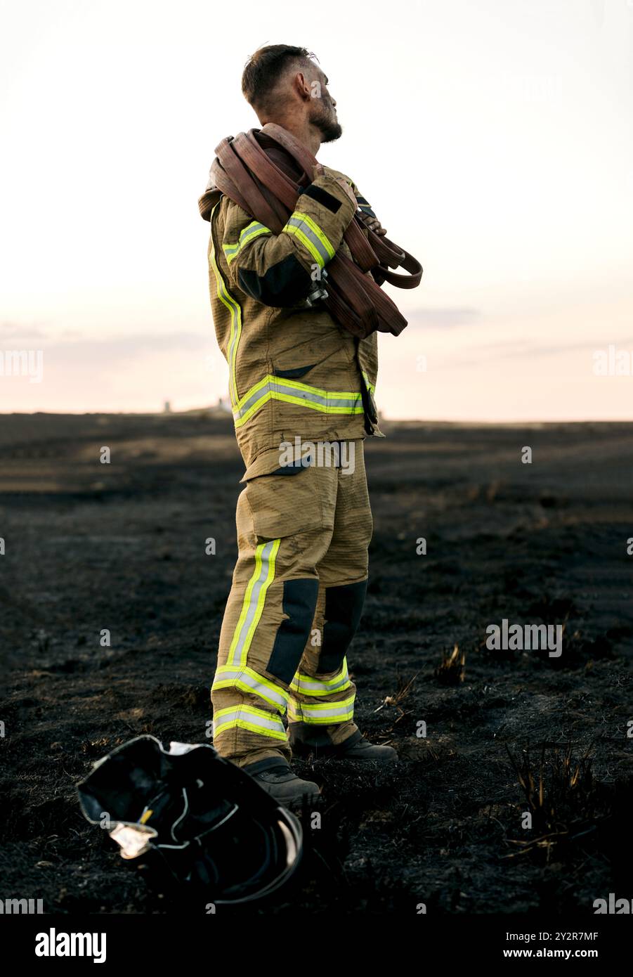 A fire fighter stands reflectively in a charred forest, holding a large ...