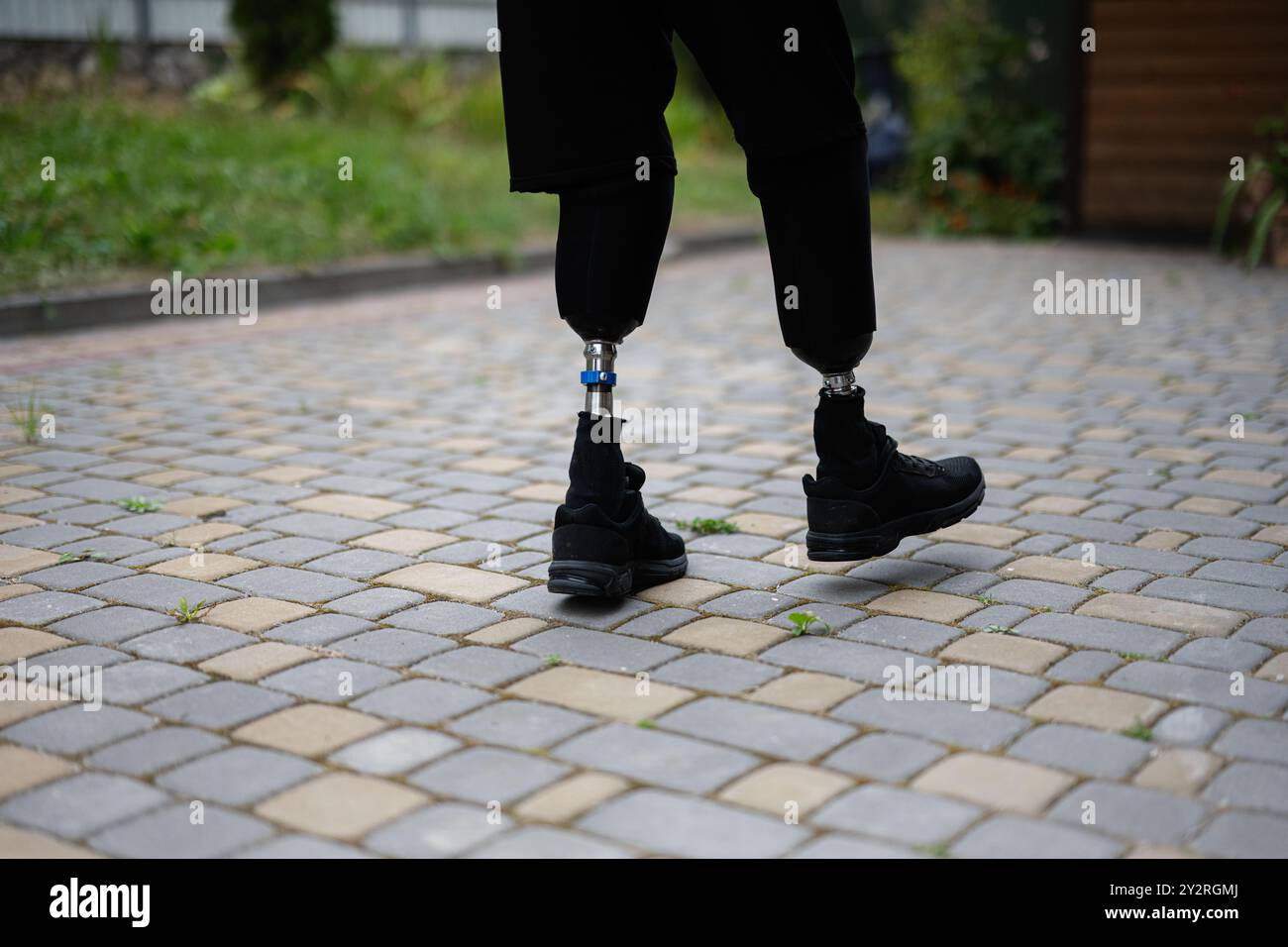 A person using prosthetic legs takes steps forward on a cobblestone ...