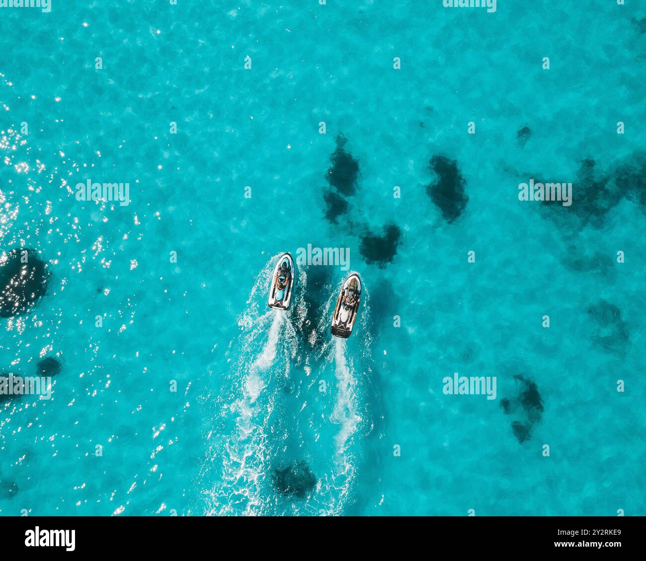 An aerial view of two jet skis on clear blue ocean water creating white ...