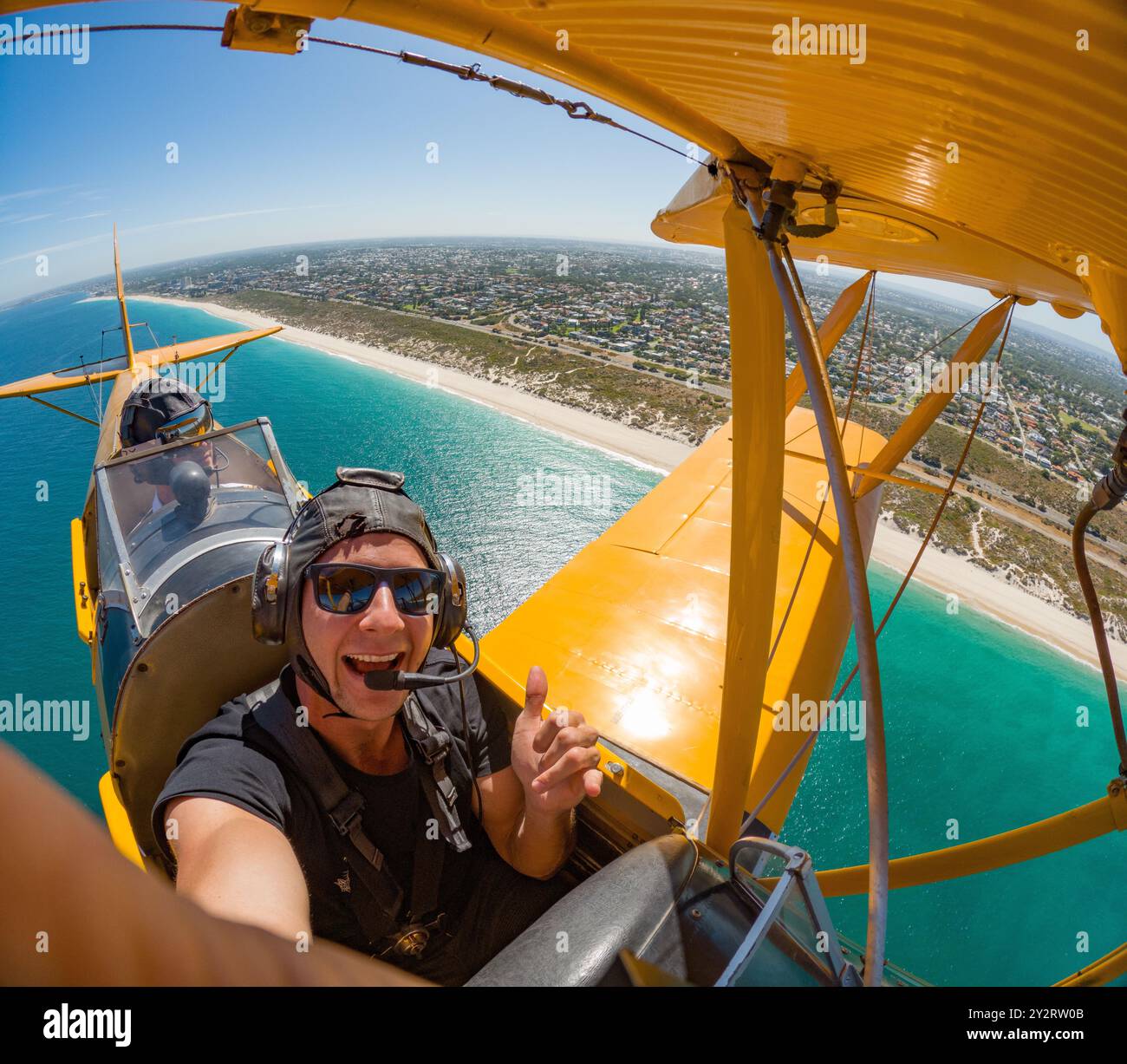 A man taking a selfie while flying in a vintage yellow biplane over a ...