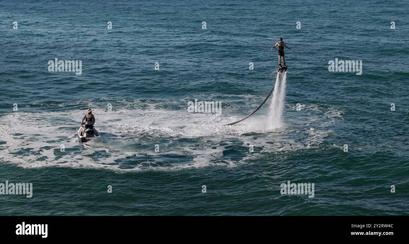 A person enjoying a water jetpack ride while another person assists on ...