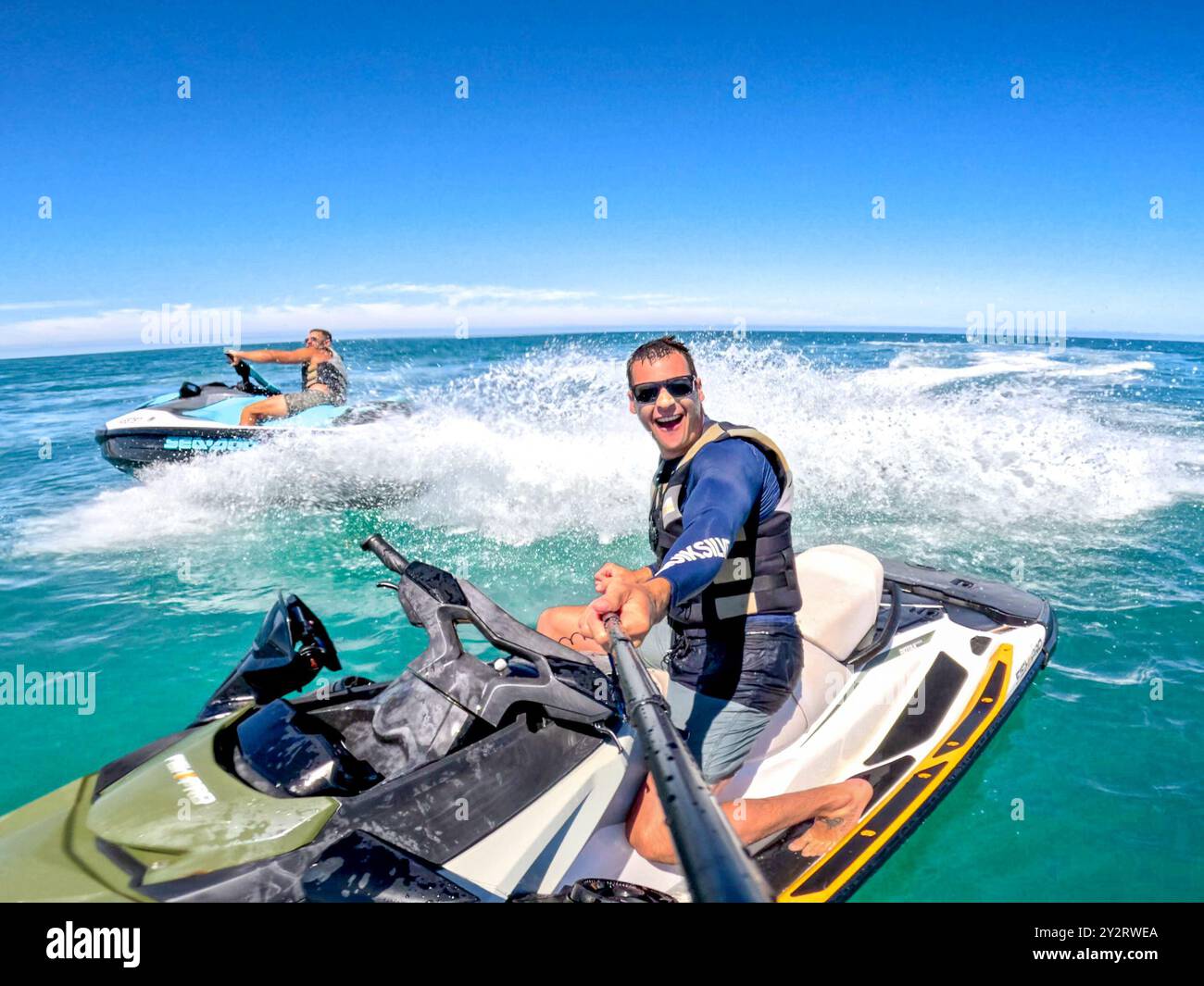 Two men riding jet skis on a clear blue ocean, capturing a fun and ...