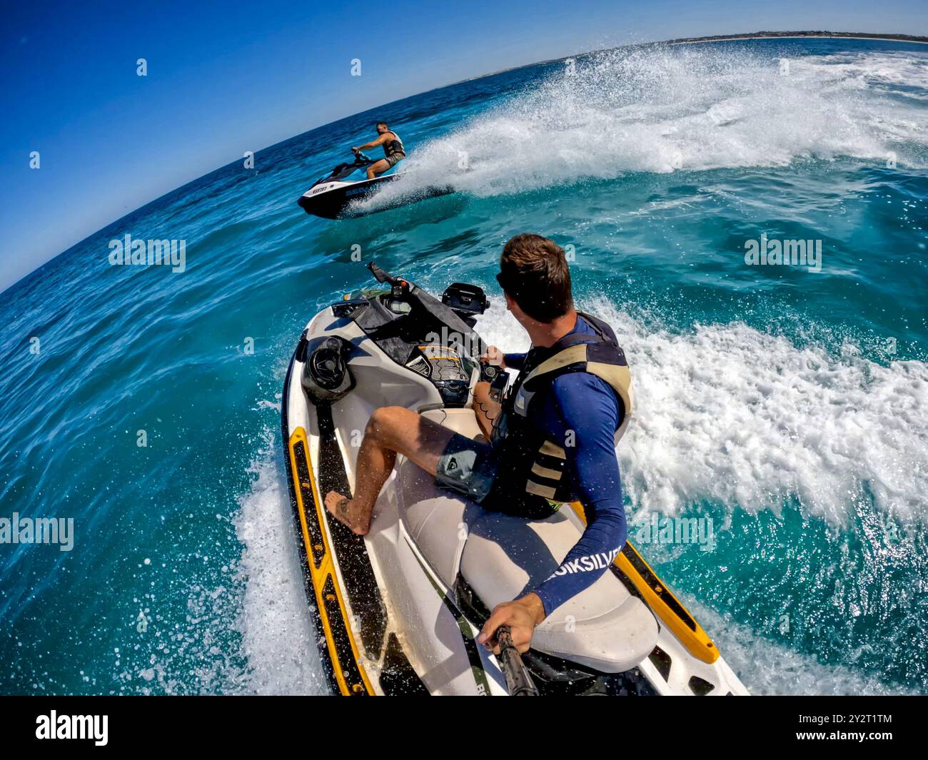 Two men riding jet skis on a clear blue ocean under a bright sunny sky ...