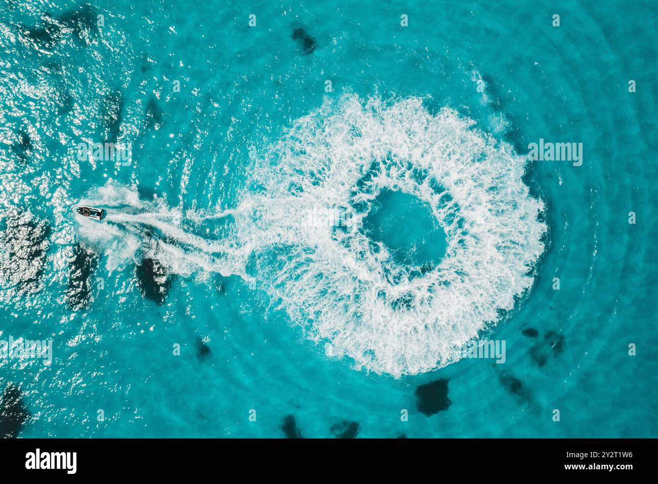 Aerial view of a jet ski creating circular waves in clear blue ocean ...
