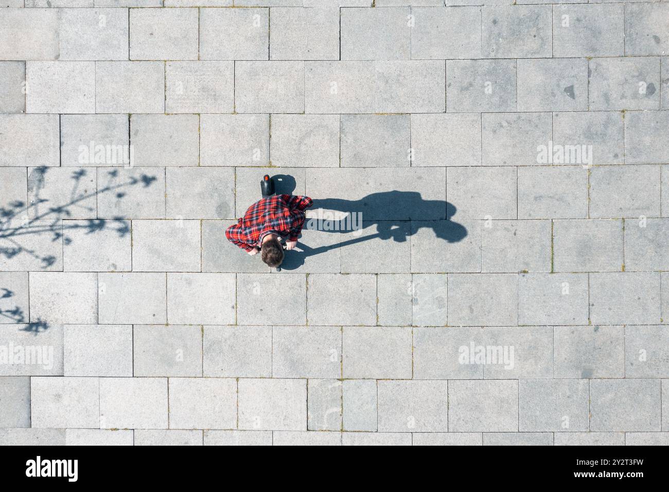 Top view of man riding electric scooter on paved surface casting shadow ...