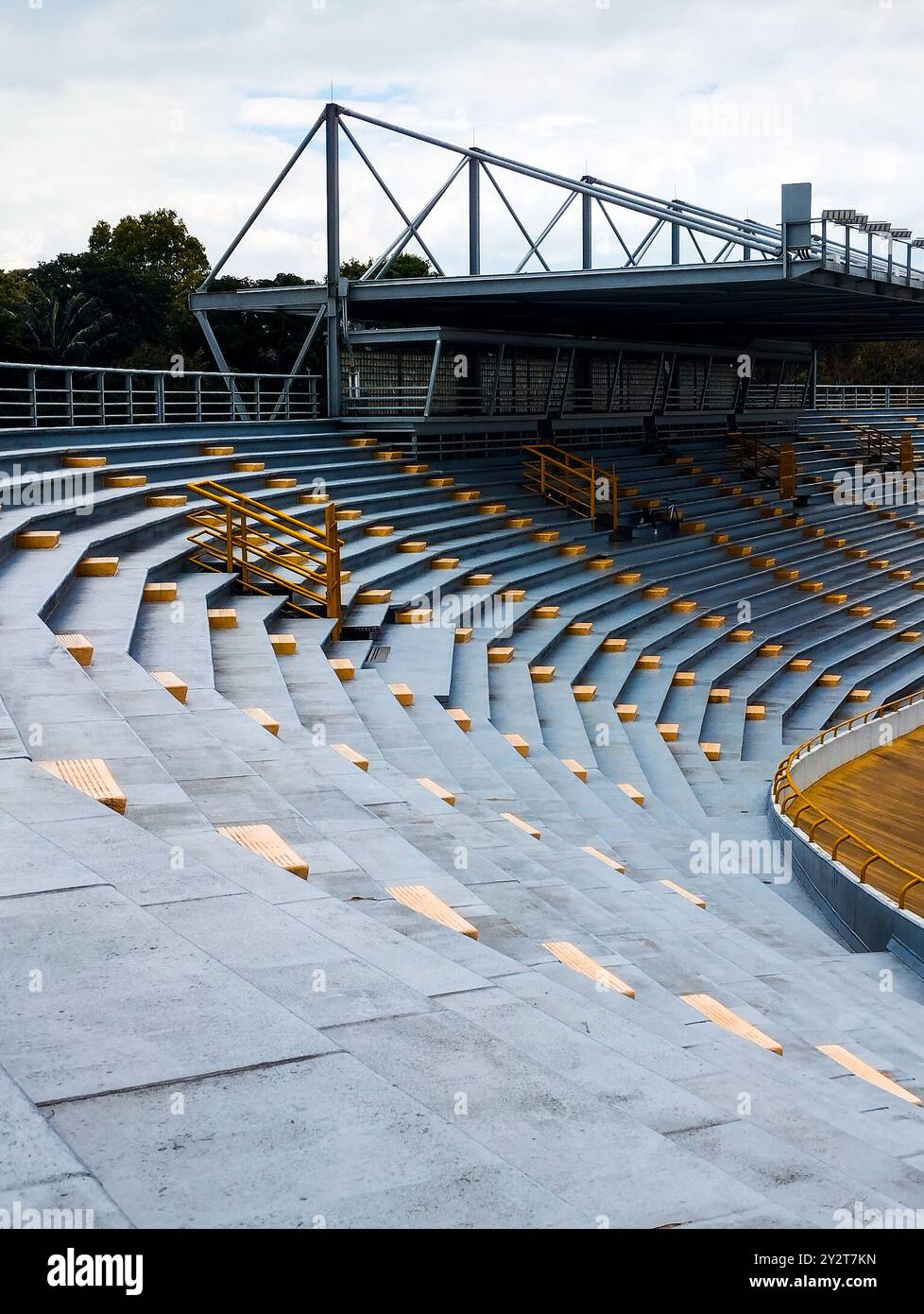 An empty outdoor stadium with tiered seating and a metal roof structure ...