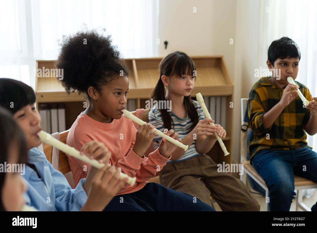 Diverse elementary students practice flutes in vibrant music classroom ...