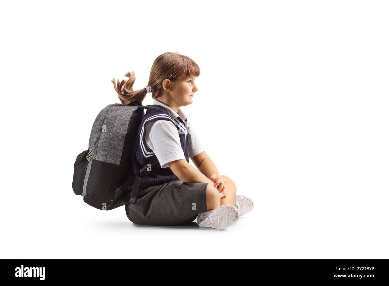 Schoolgirl in a uniform with a backpack sitting on the ground isolated ...