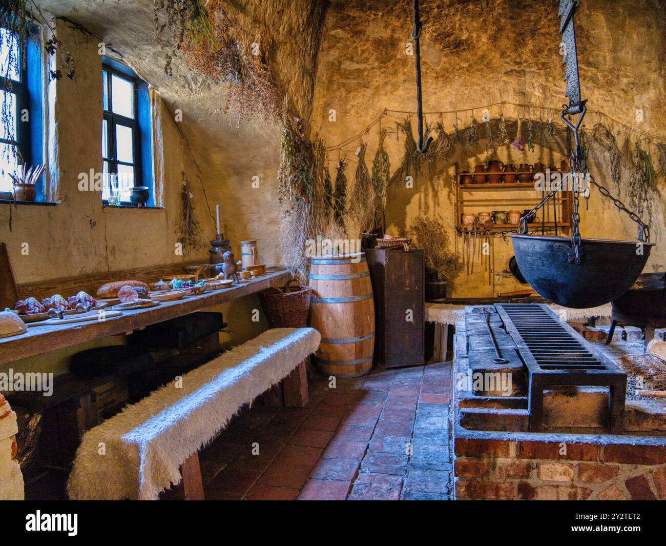 A rustic medieval kitchen with a large cauldron, wooden benches, and ...