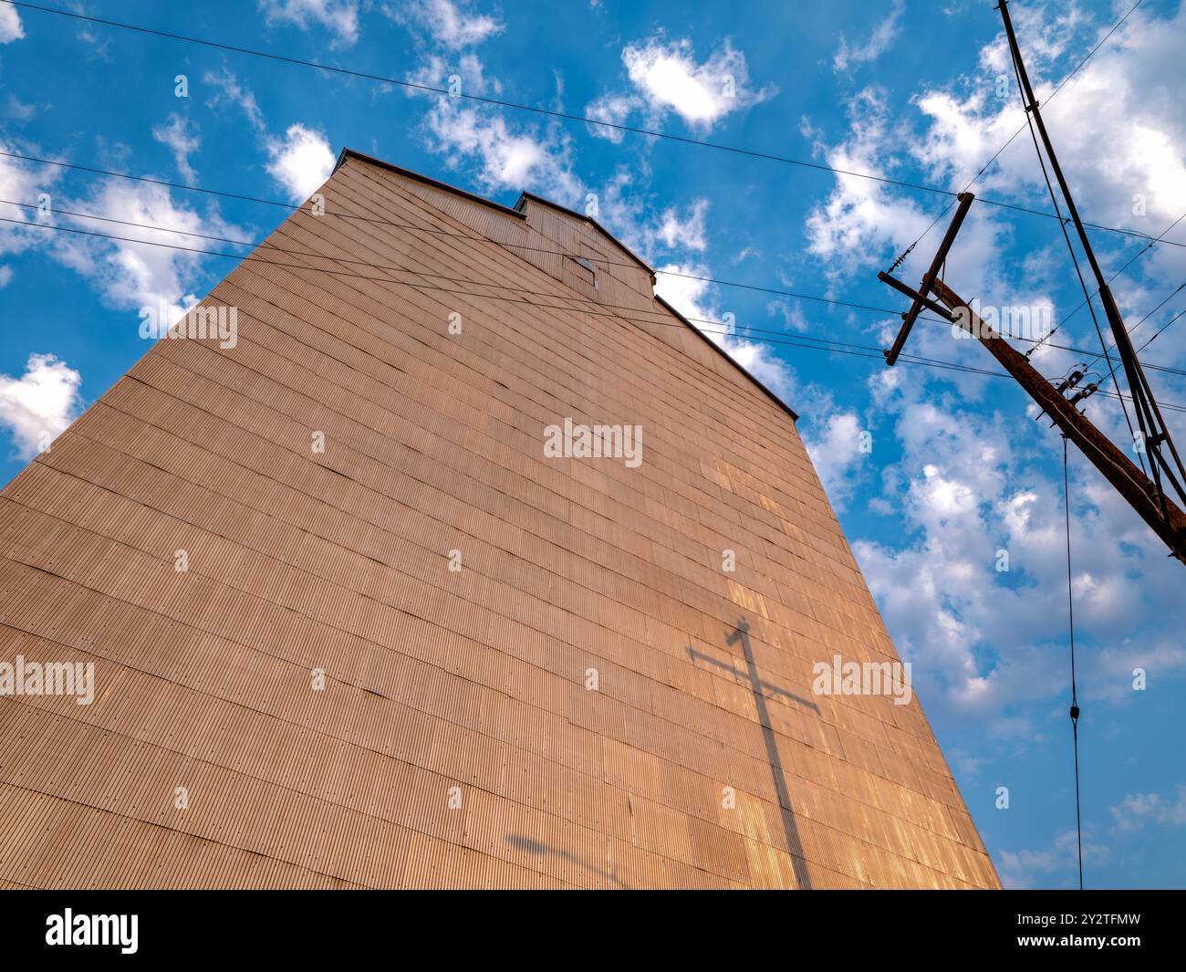 Power poles cast shadows on the corrugated metal wall of an old grain ...