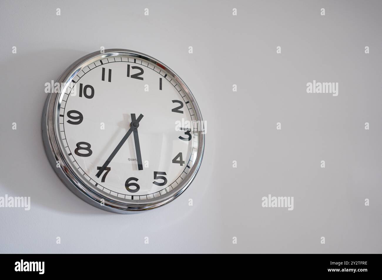 Round analog clock hanging on white wall. Shows clean and modern style ...
