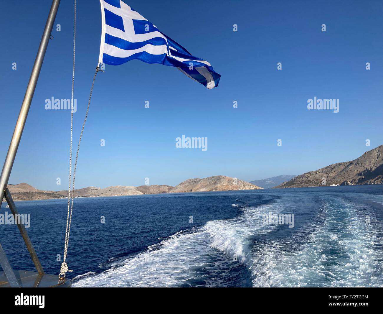 A Greek flag waving on a boat with a view of the Aegean Sea and distant ...