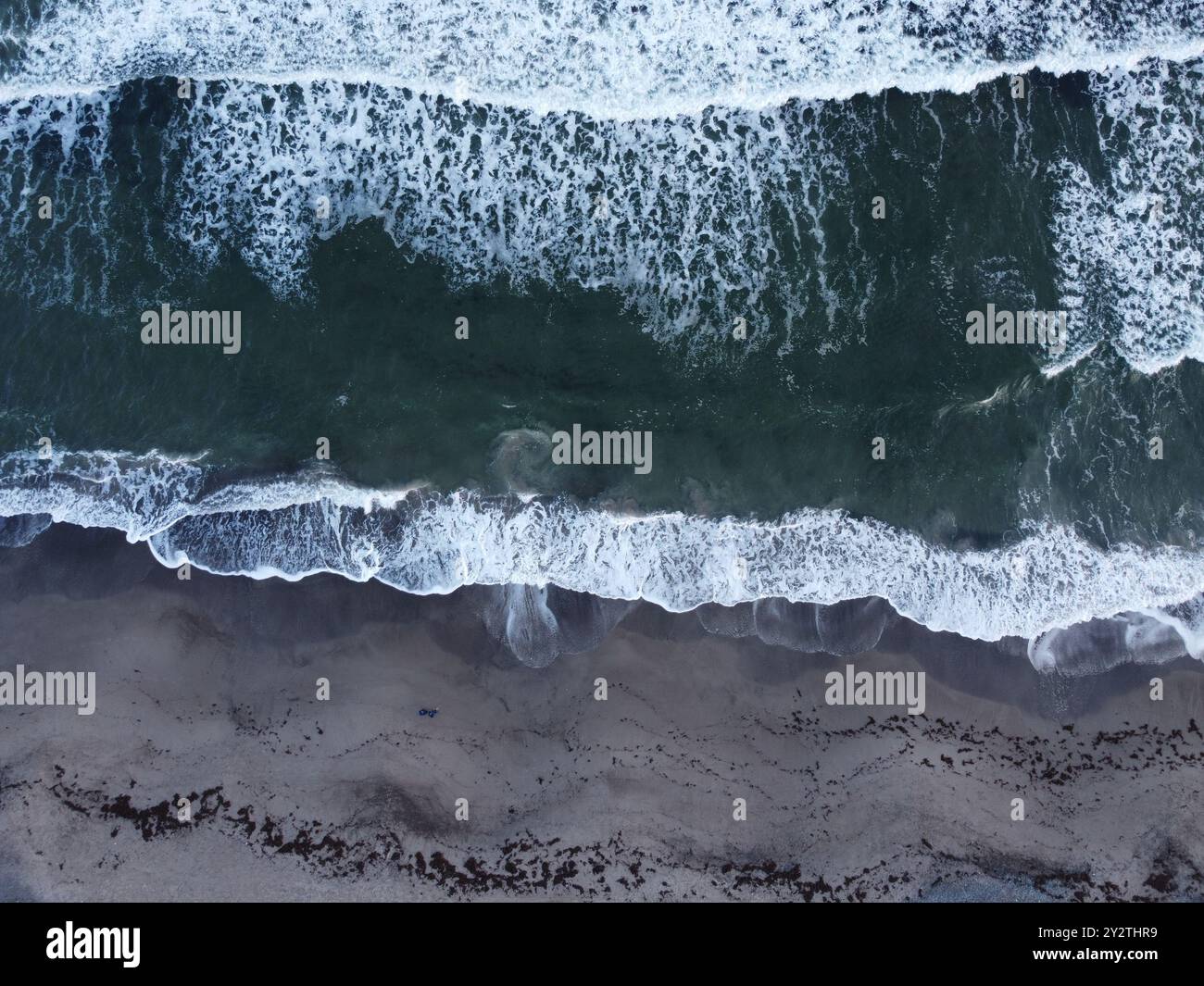 Aerial view of ocean waves crashing on a sandy beach with seaweed ...