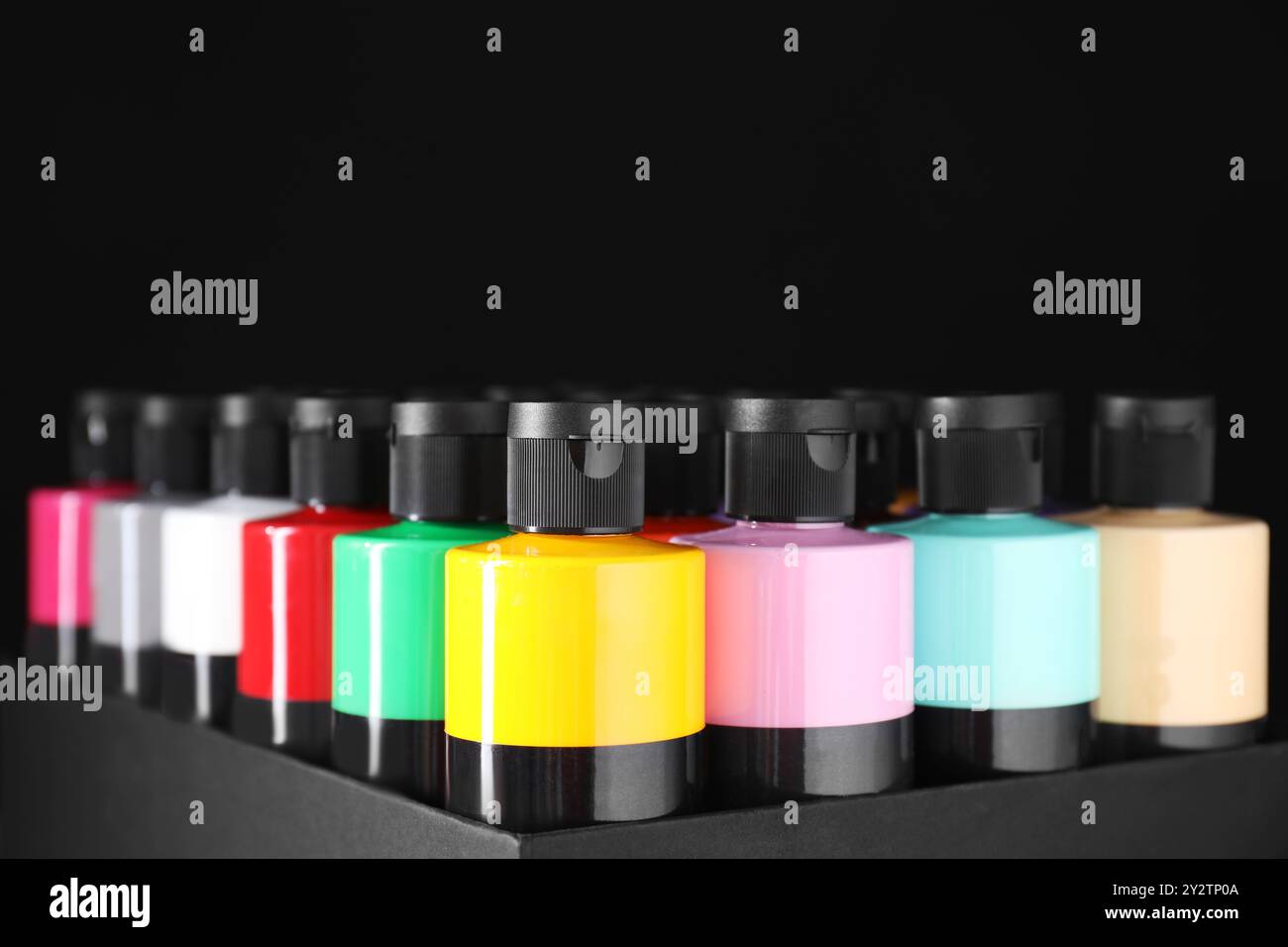 Acrylic paints of different colors in bottles against black background ...