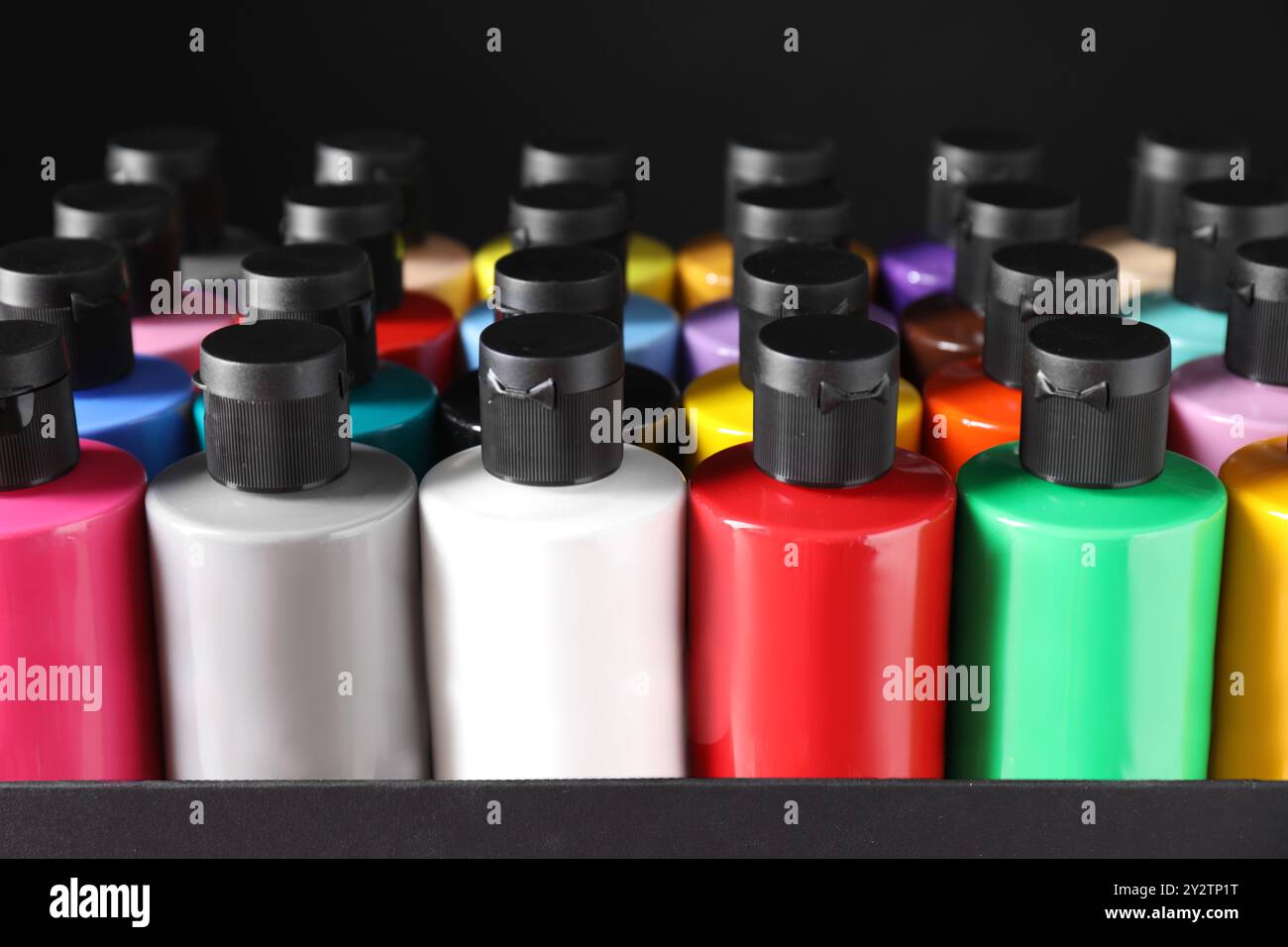 Acrylic paints of different colors in bottles against black background ...