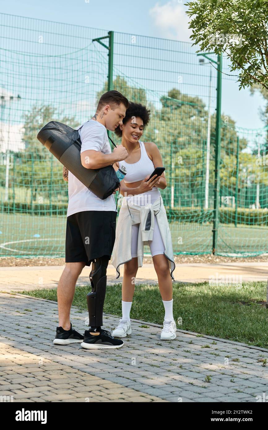 A young woman and a tattooed man with a prosthetic leg share workout tips, looking at smartphone ...