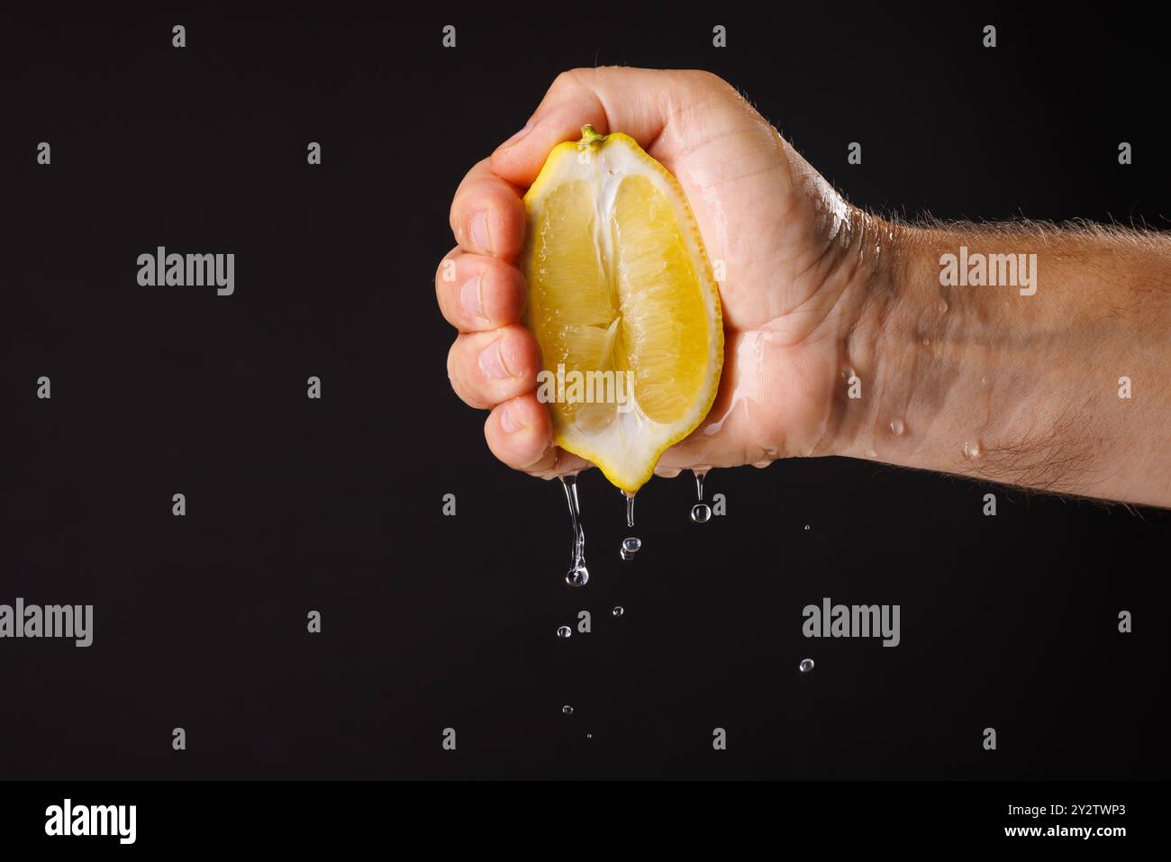 A hand squeezing a lemon, with juice dripping down. The background is ...