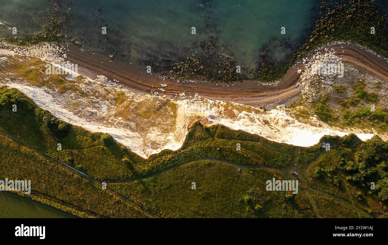 Aerial view of a coastal cliff with green fields and clear water below ...