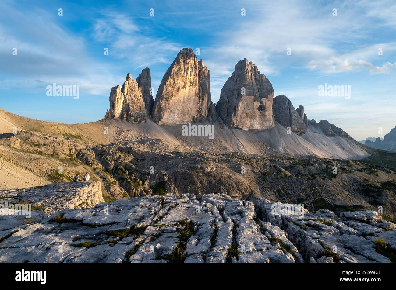 Two people sitting on a rock formation with a stunning view of Tre Cime ...