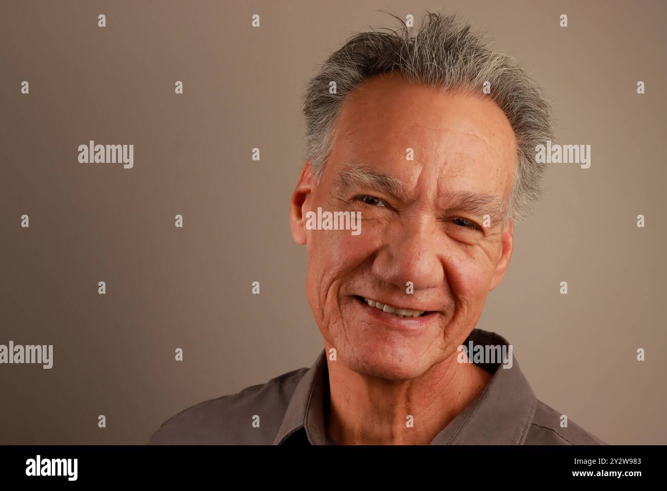 A portrait of a senior Hispanic man smiling against a neutral ...