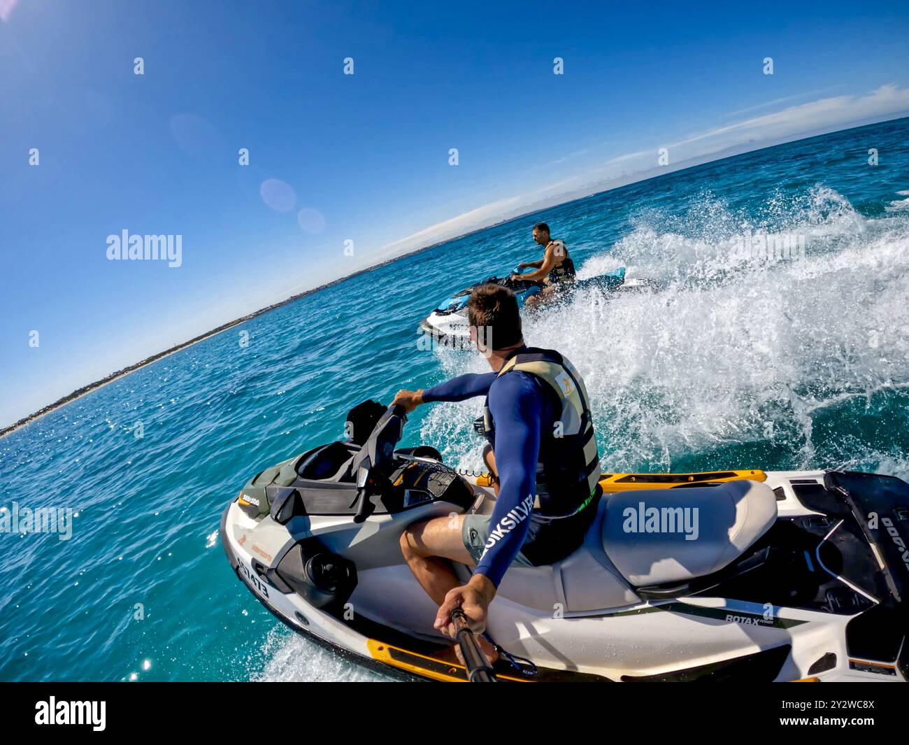 Two men riding jet skis on a clear blue ocean under a bright sunny sky ...