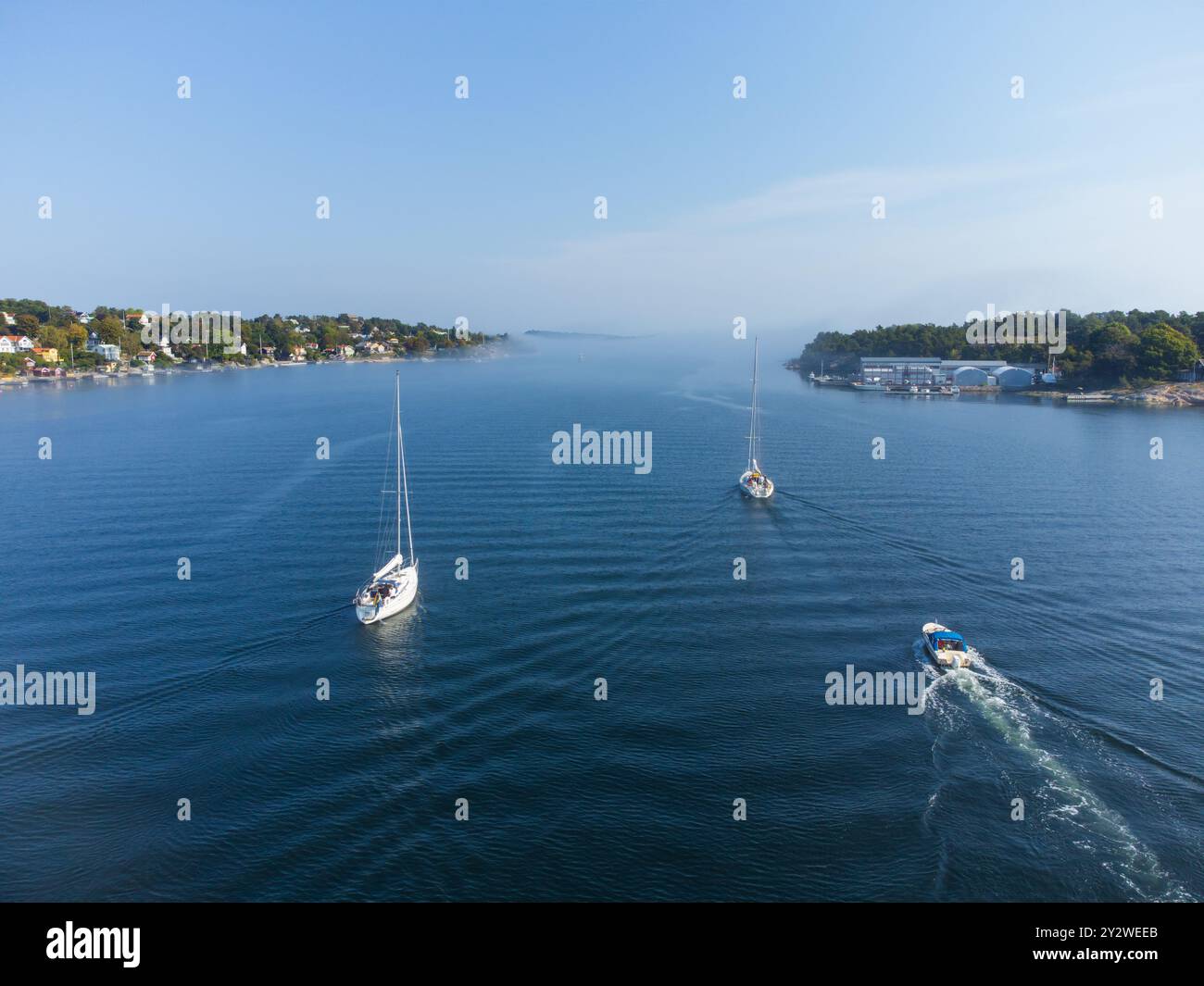 Sailboats and a boat cruising on the sea with morning fog rolling over ...