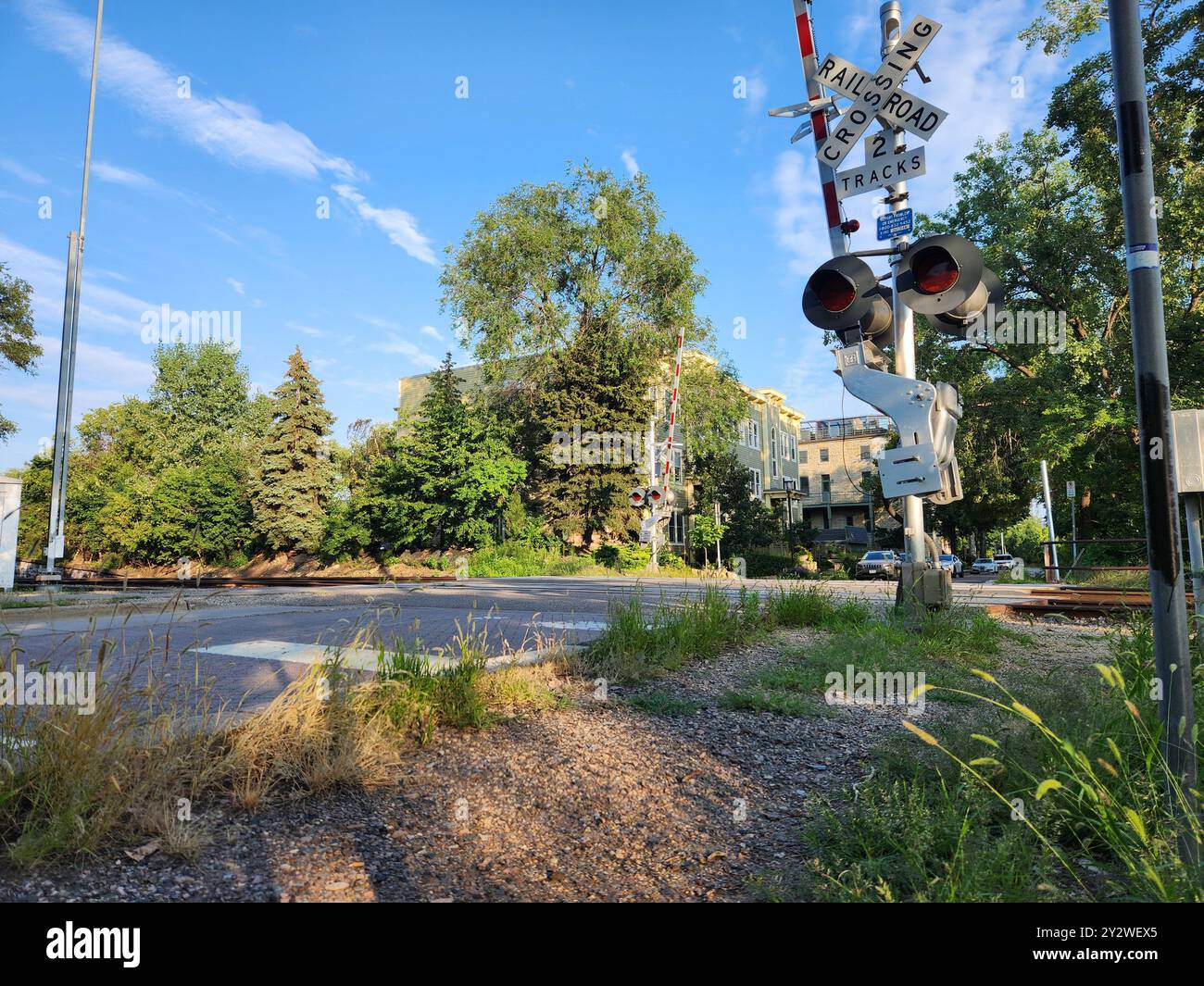 A railroad crossing with signal lights and barriers in a suburban area ...