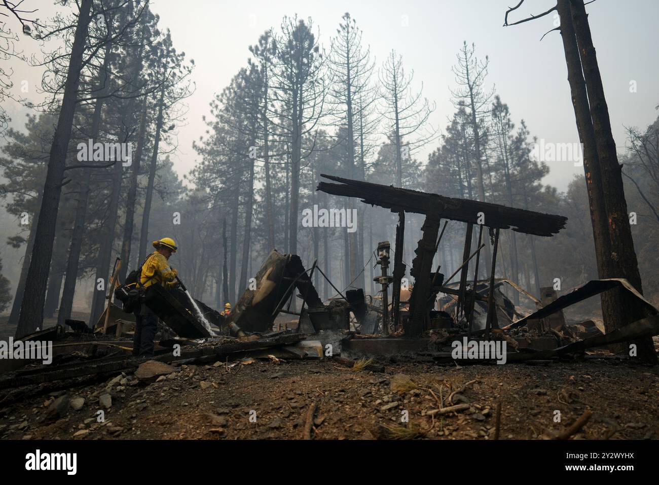 A firefighter hoses down hot spots on a fire-ravaged property while ...