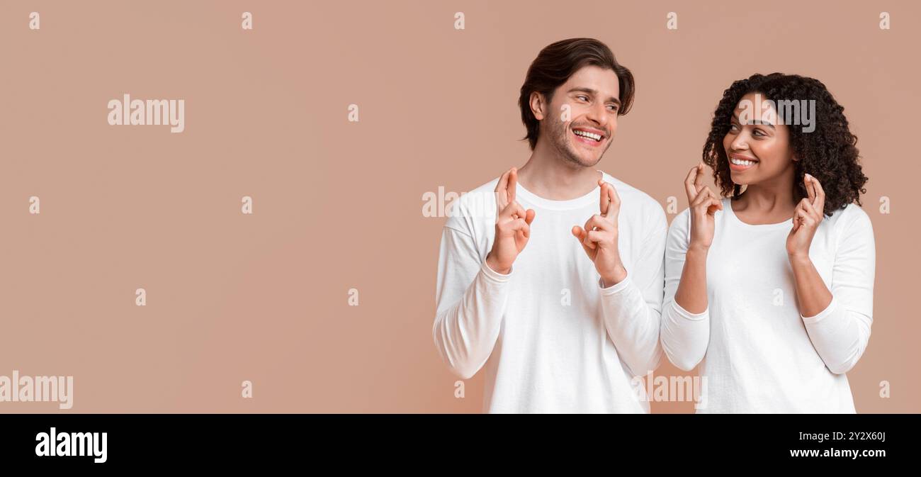 Happy interracial couple crossing fingers, pleading for something Stock ...