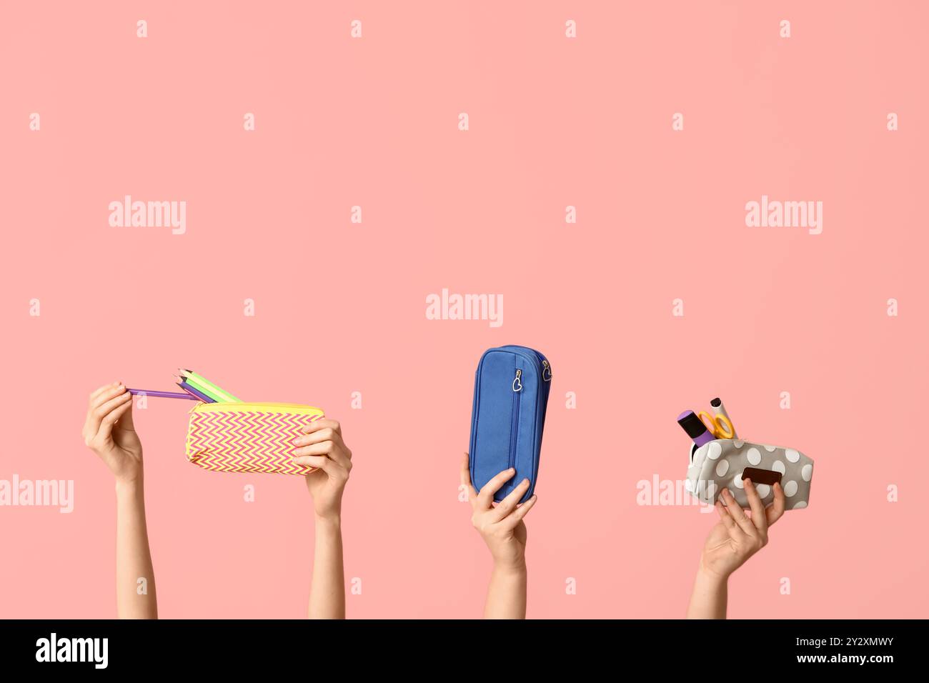 Female hands holding pencil cases with stationery on pink background ...