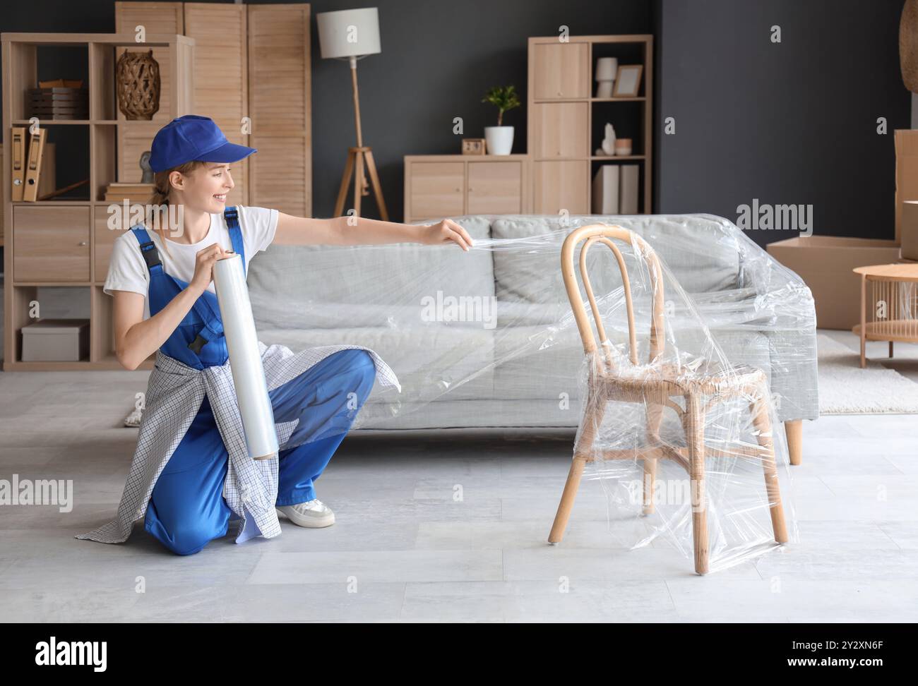 Female worker wrapping chair with stretch film in room Stock Photo - Alamy