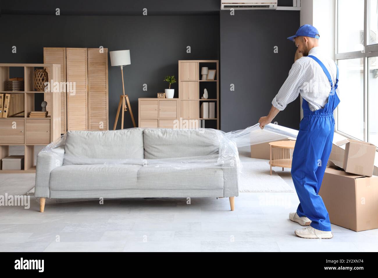 Male worker wrapping sofa with stretch film in room Stock Photo - Alamy