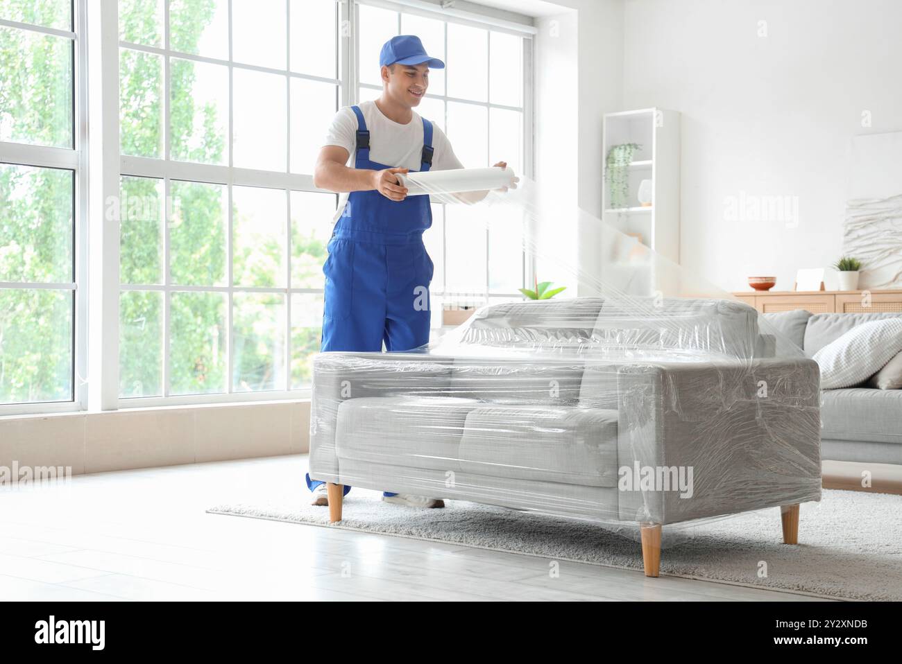 Male worker wrapping sofa with stretch film in room Stock Photo - Alamy